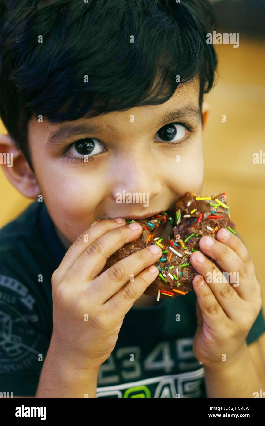 cute indian kid eating donut in close up Stock Photo - Alamy