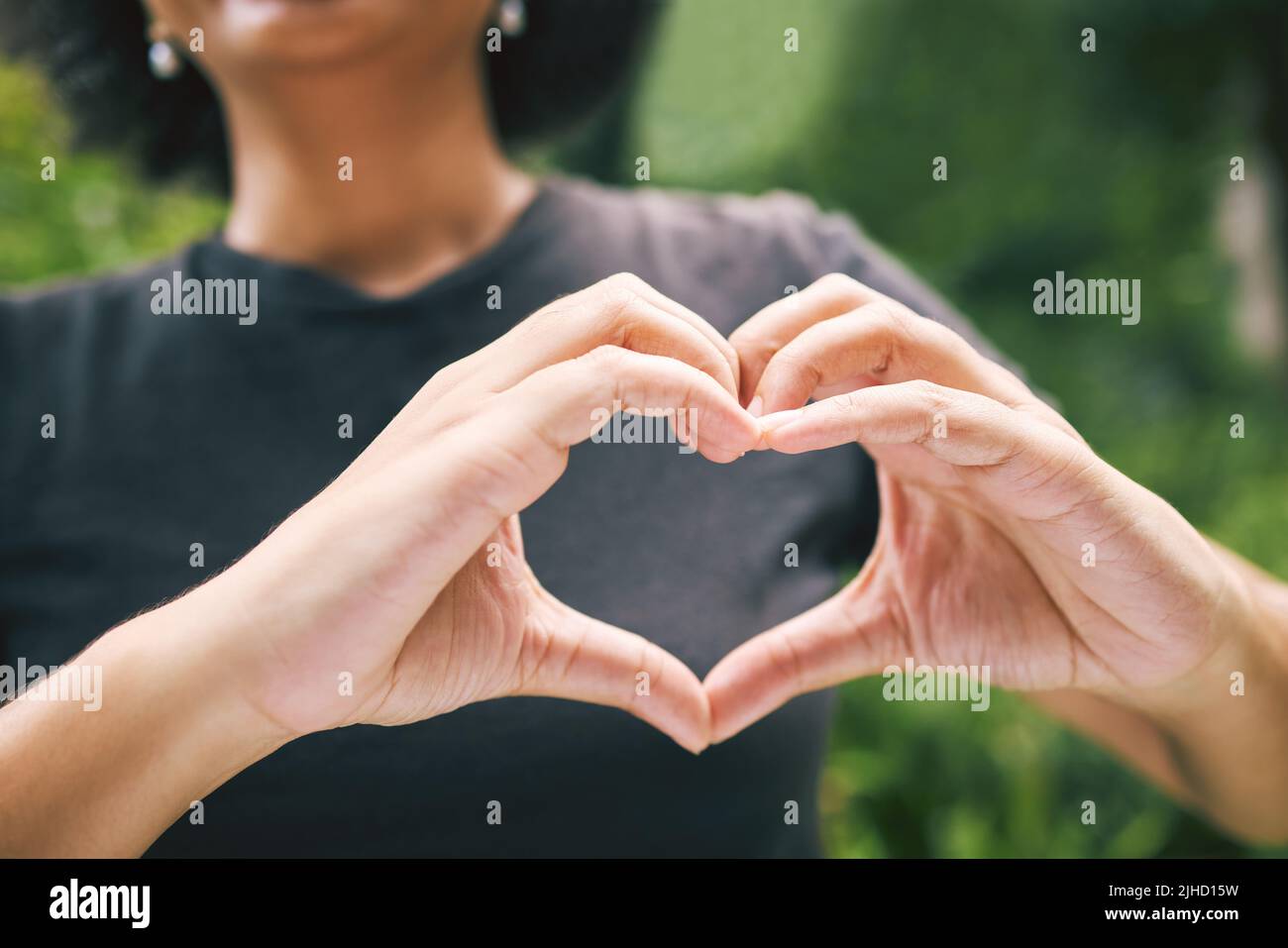 Closeup of a person showing a heart gesture outside in nature. A female ...