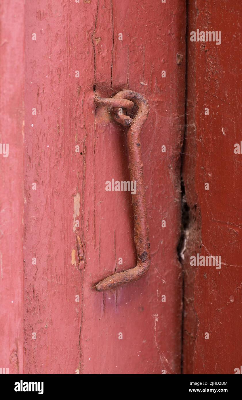 Closeup of textured red door with a rusty metal hook. Bright wooden ...