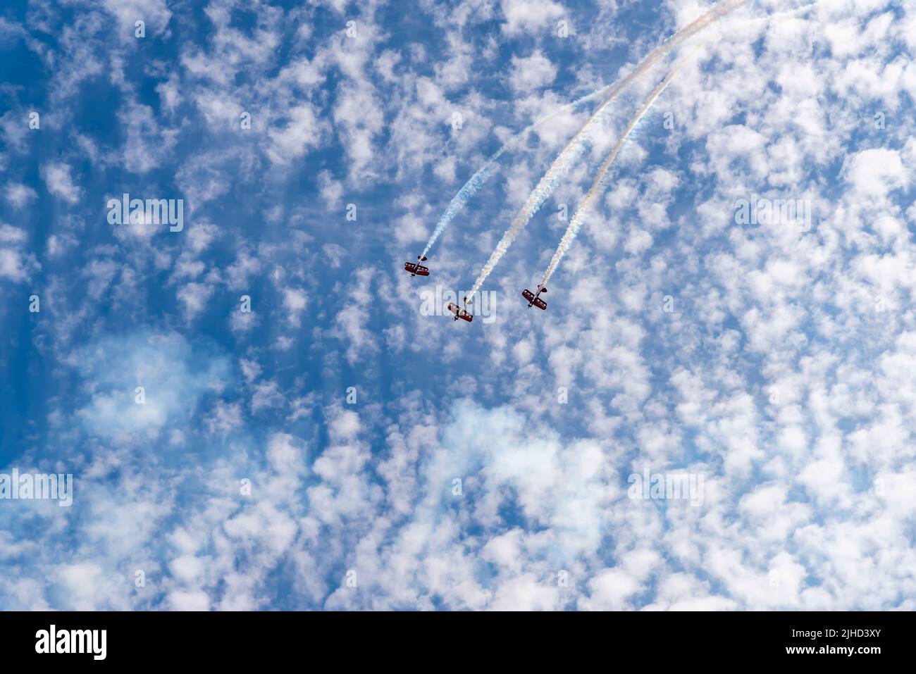 three red planes fly down and show aerobatics in a blue sky with clouds ...