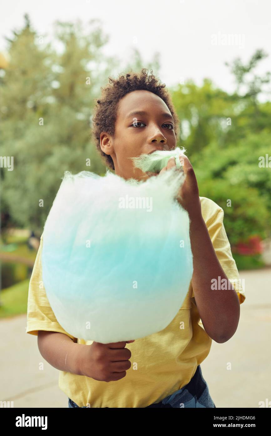 African boy eating cotton candy while walking outdoors in the park ...