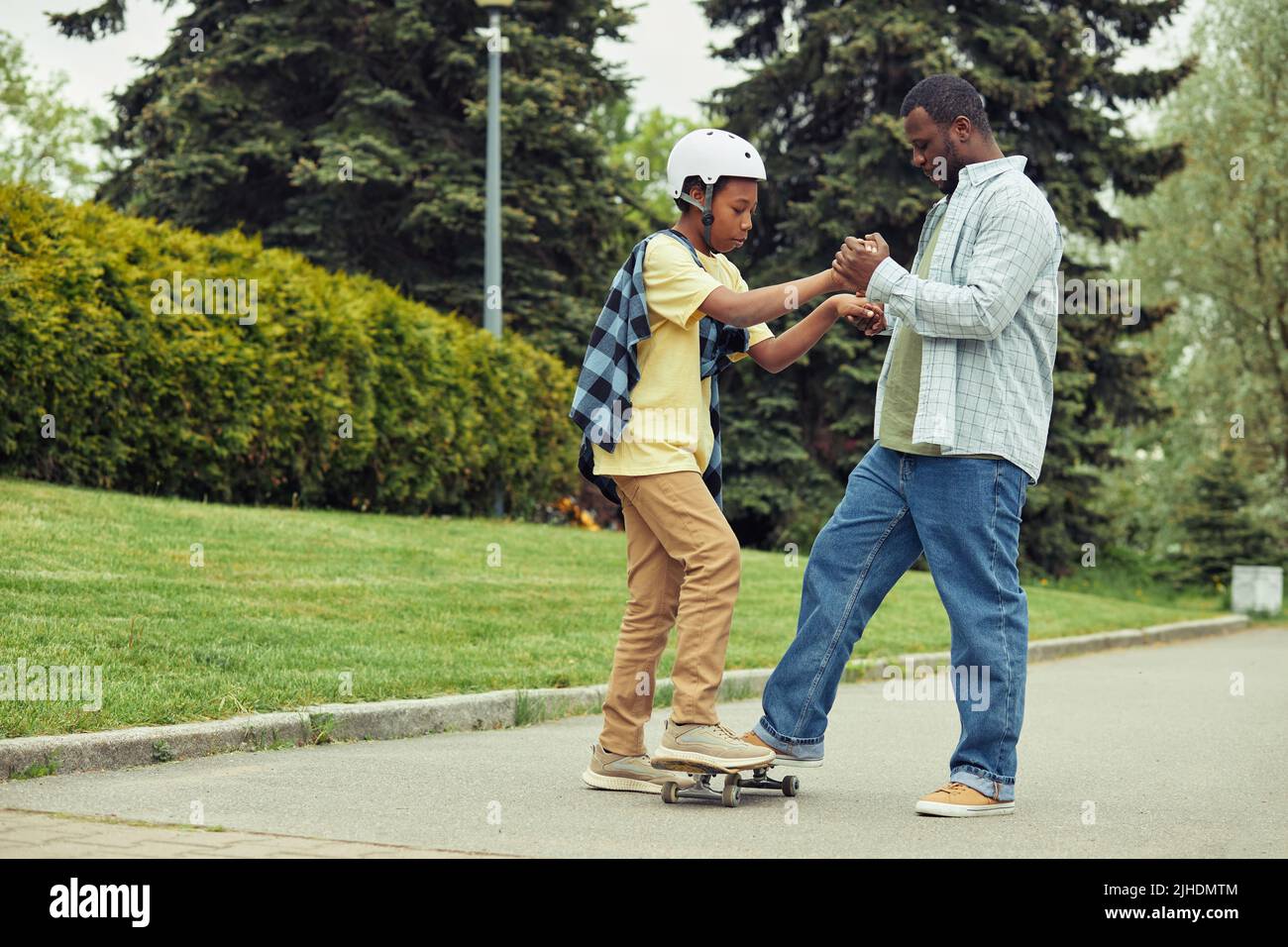 African dad helping his son to stand on skateboard and teaching him to ...