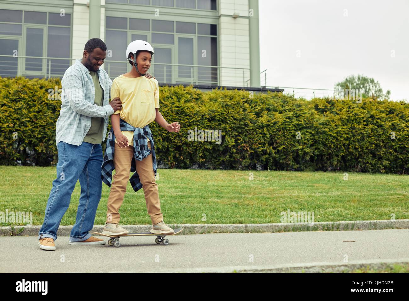 African happy dad pushing his son while he standing on skateboard, he ...