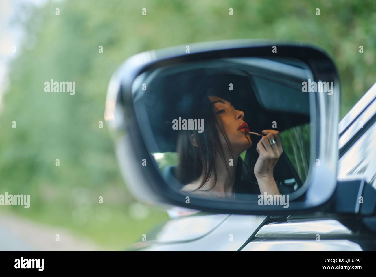 Reflection in rear view mirror of a woman applying lipstick while ...