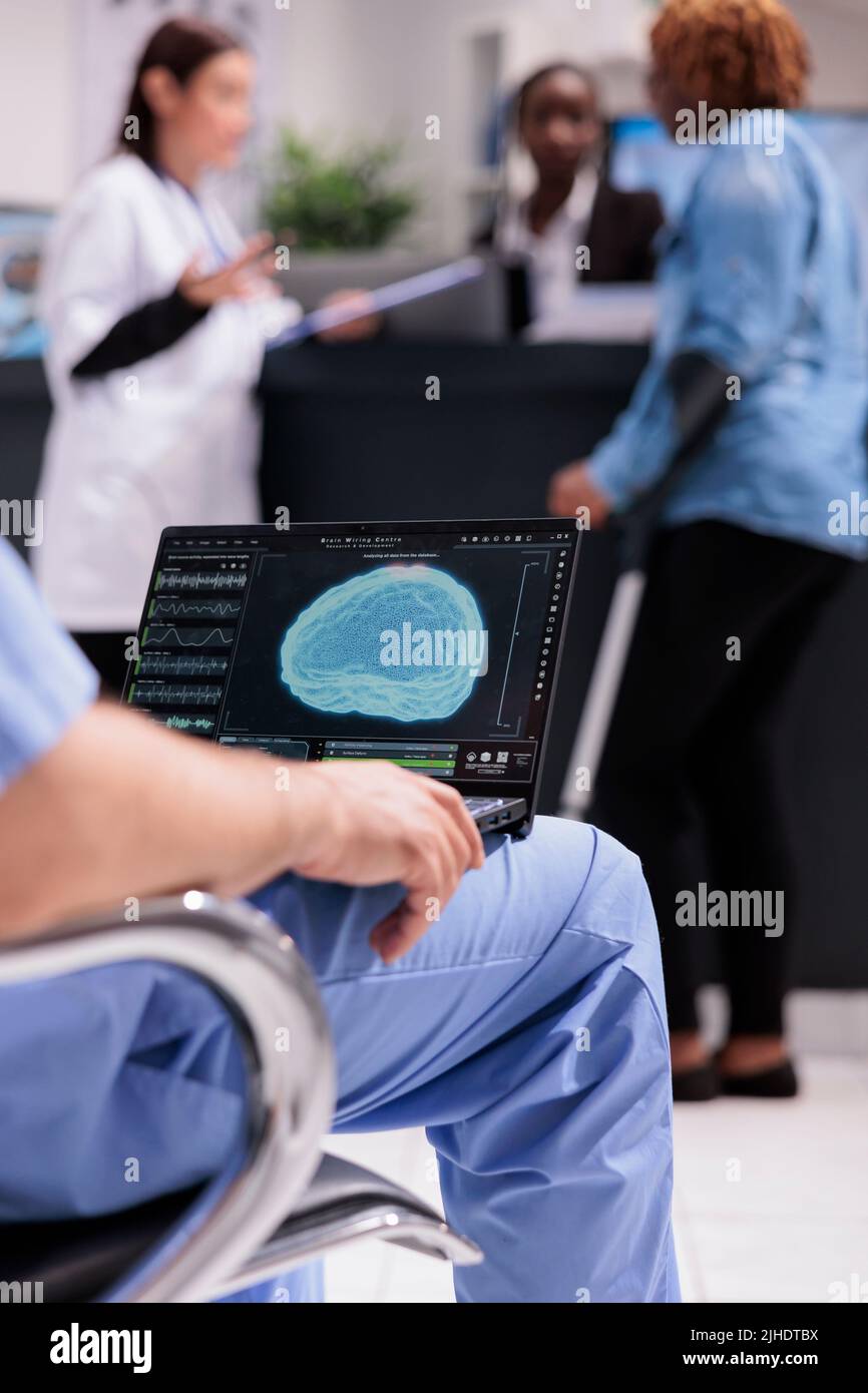 Male nurse analyzing brain animation on laptop, sitting in waiting room ...