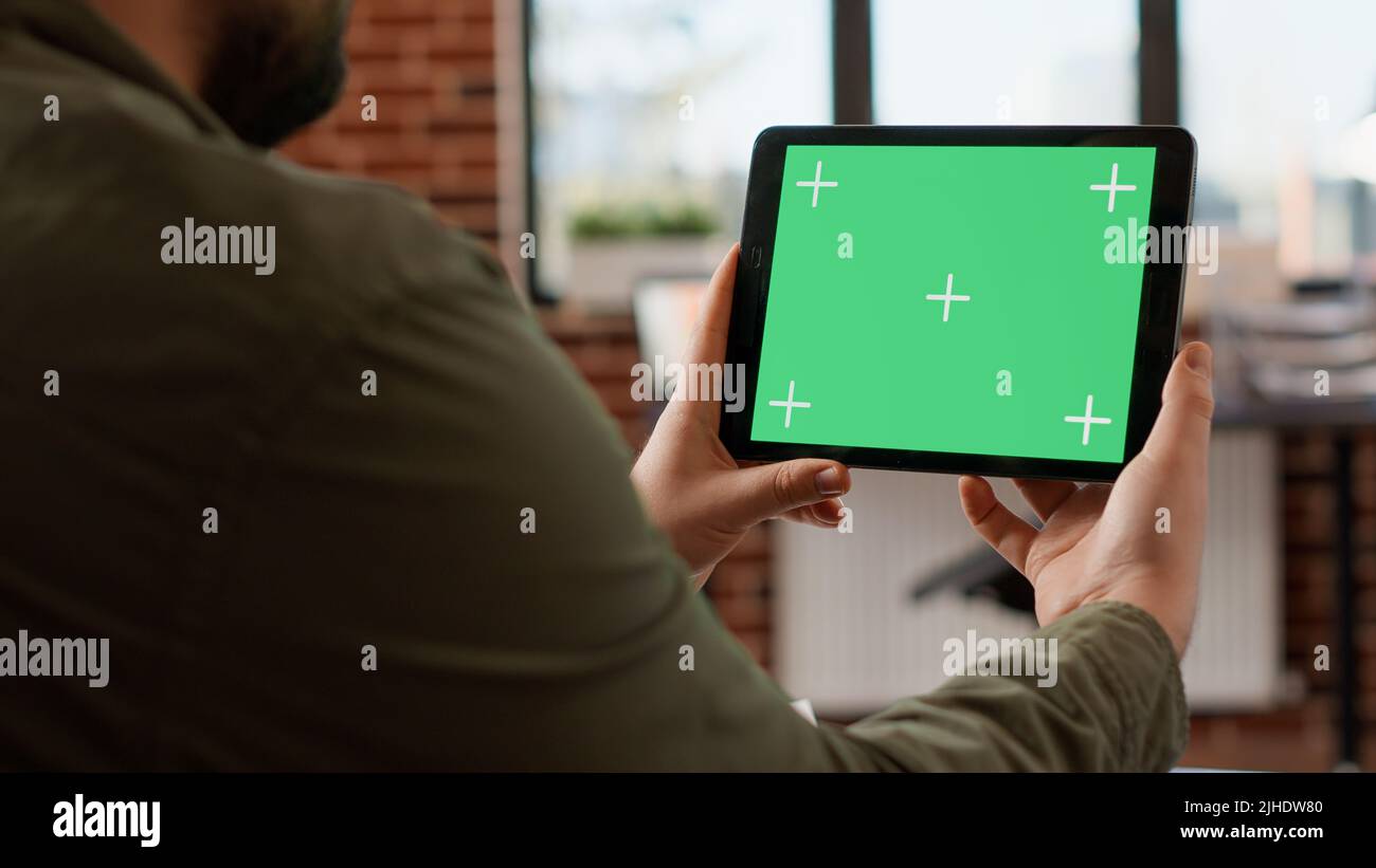 Office worker holding horizontal greenscreen on tablet, analyzing chroma key display with ...