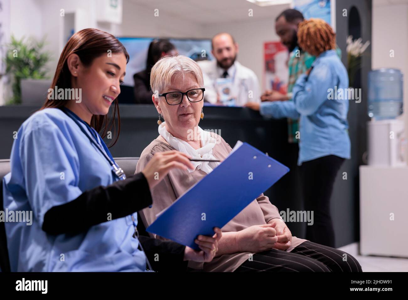 Asian nurse explaining diagnosis to elderly patient, sitting in waiting ...