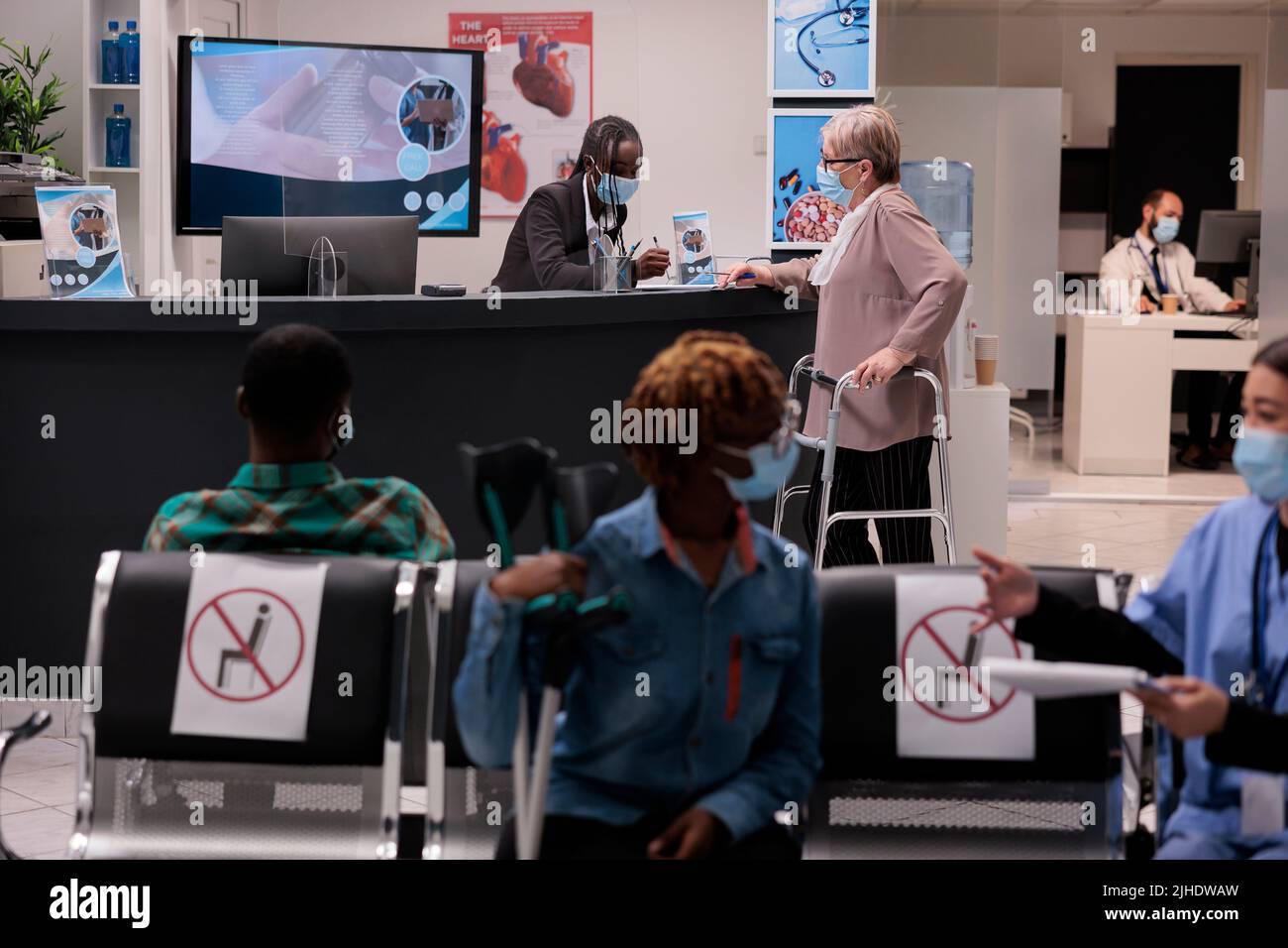 Senior patient with walk frame talking to receptionist at hospital ...
