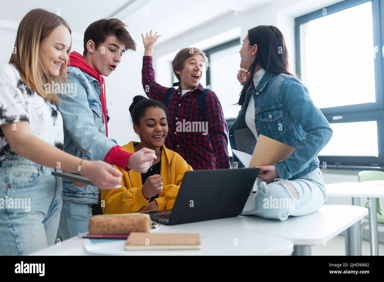 High school students sitting together at desk and using laptop and ...