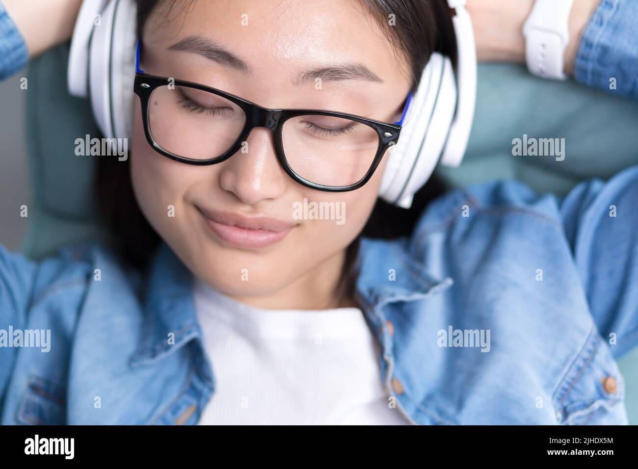 Young beautiful Asian woman listening to music in headphones, closing ...