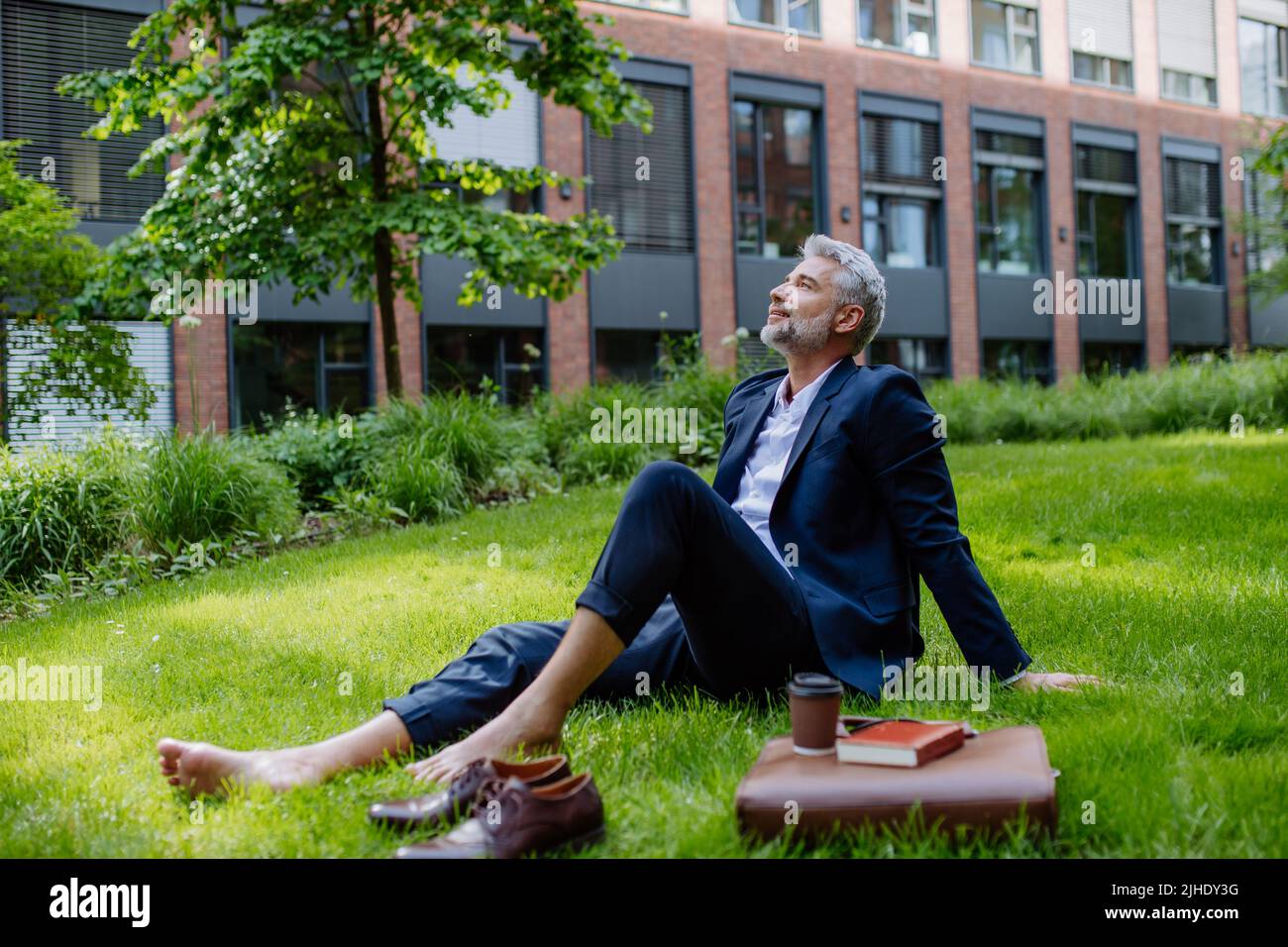 Mature businessman resting and sitting barefoot in park, feeling free ...