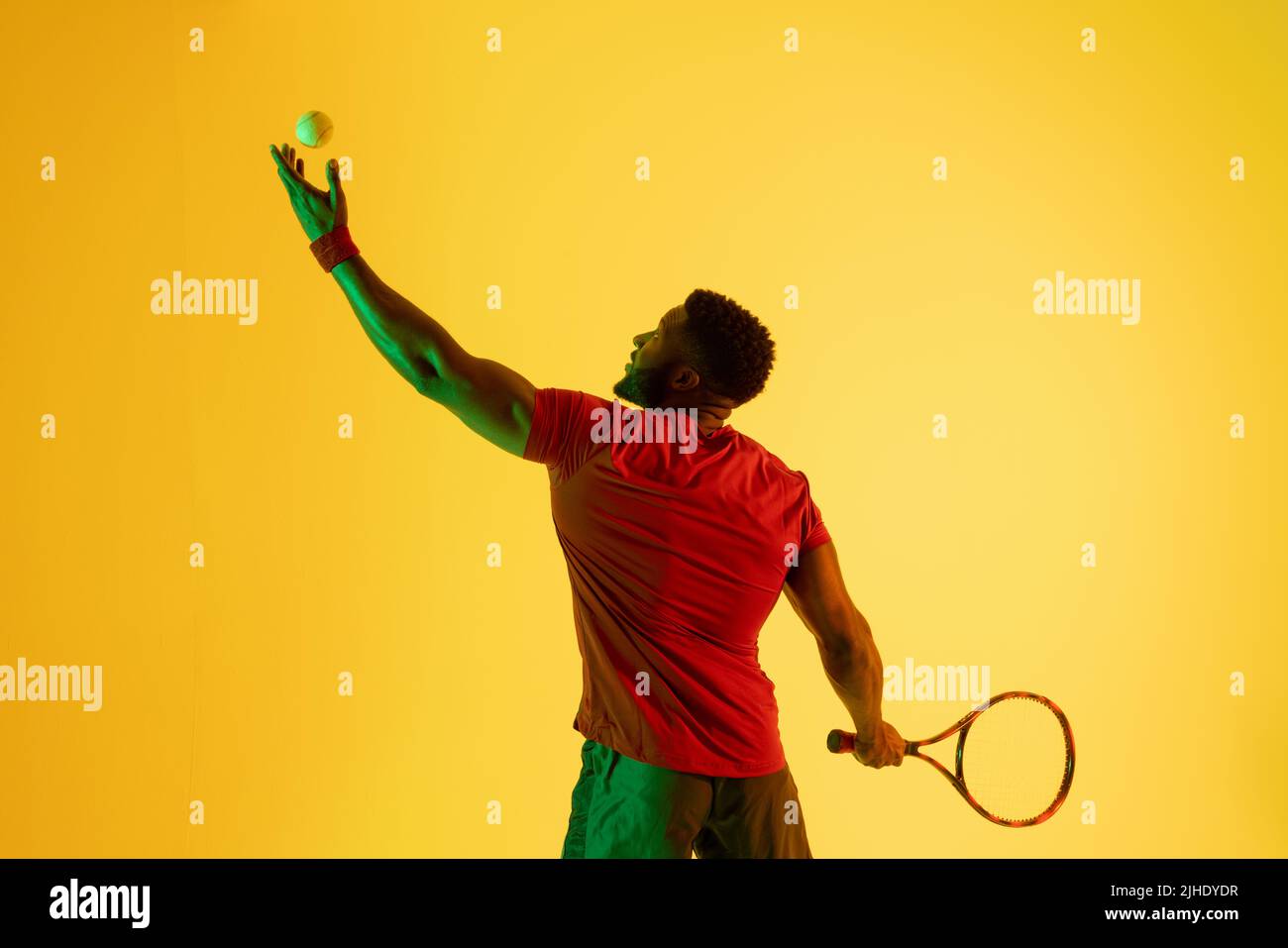Image of happy african american male tennis player in yellow lighting ...