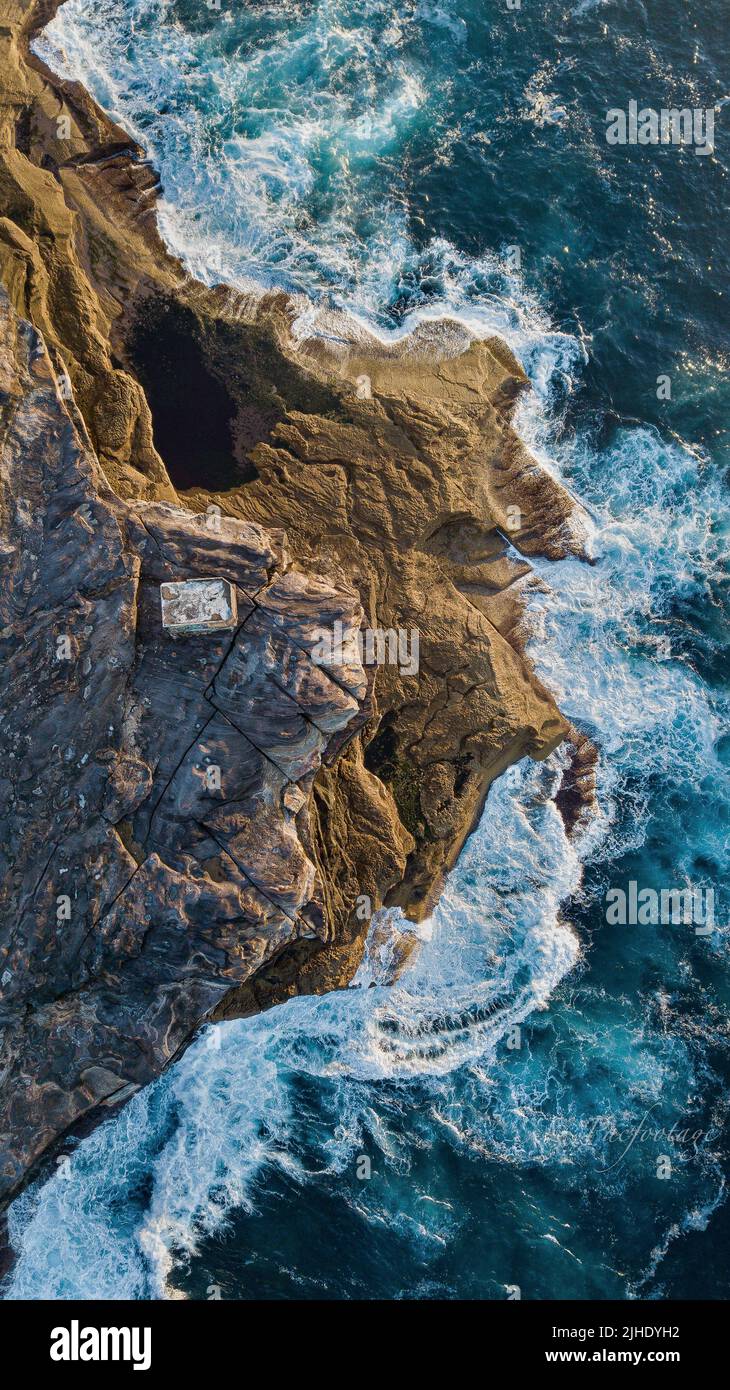 Aerial drone top view of the wavy blue sea hitting the rocky cliffs on ...