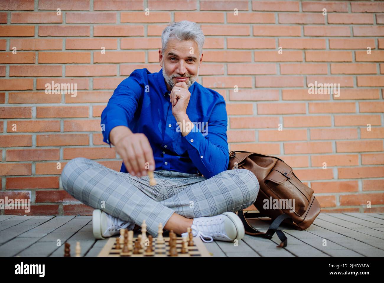 Successful happy businessman sitting in city street and playing chess ...