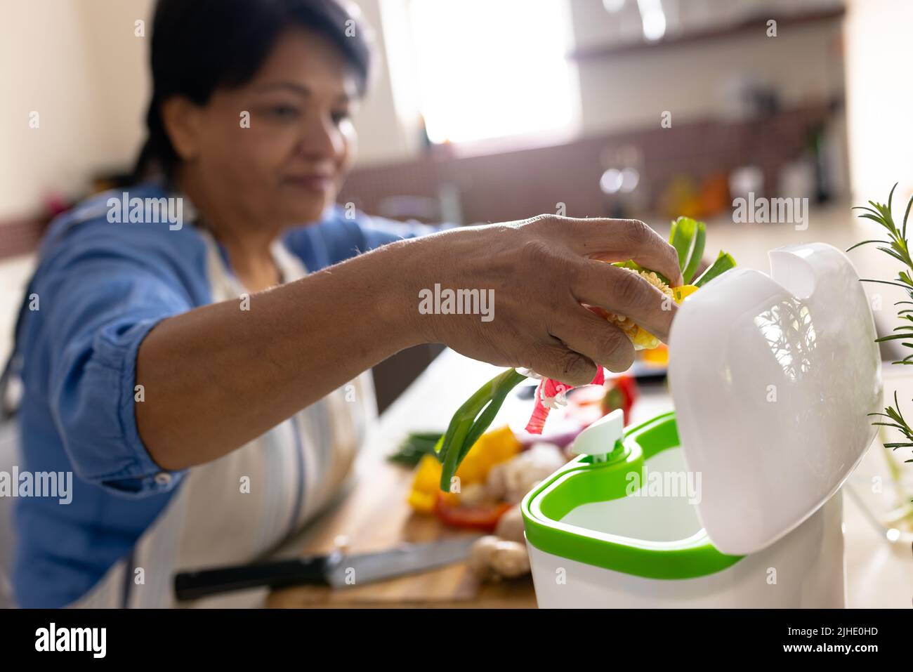 Biracial mature woman throwing vegetables waste in recycling bin while ...