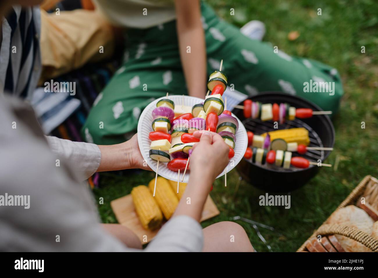 A close-up of young friends putting corn and skewers on grill and ...