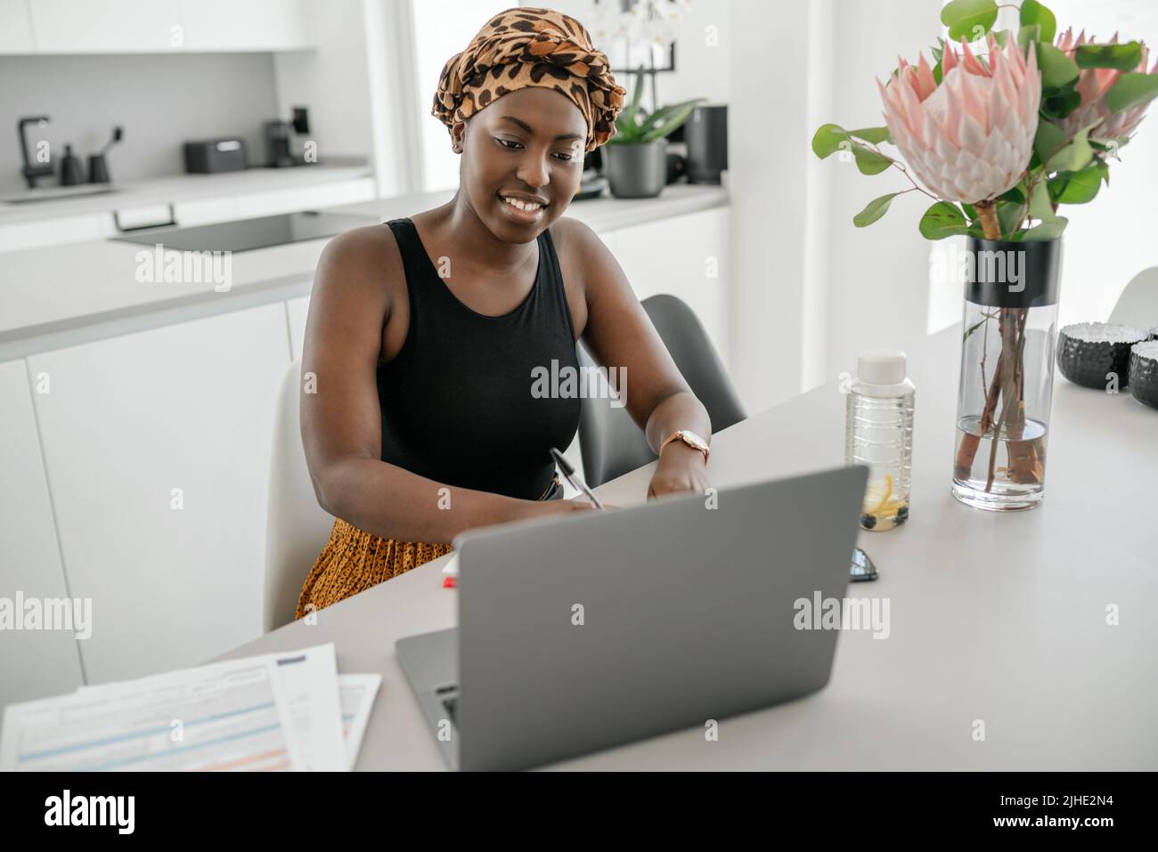 African woman working from home, going through paperwork and writing ...