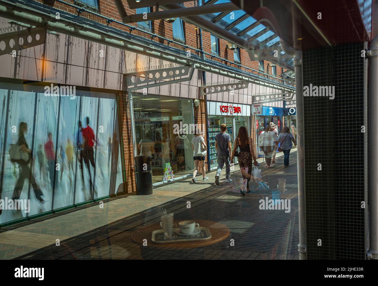 A shopping centre arcade, the reflections in a large shop window with ...