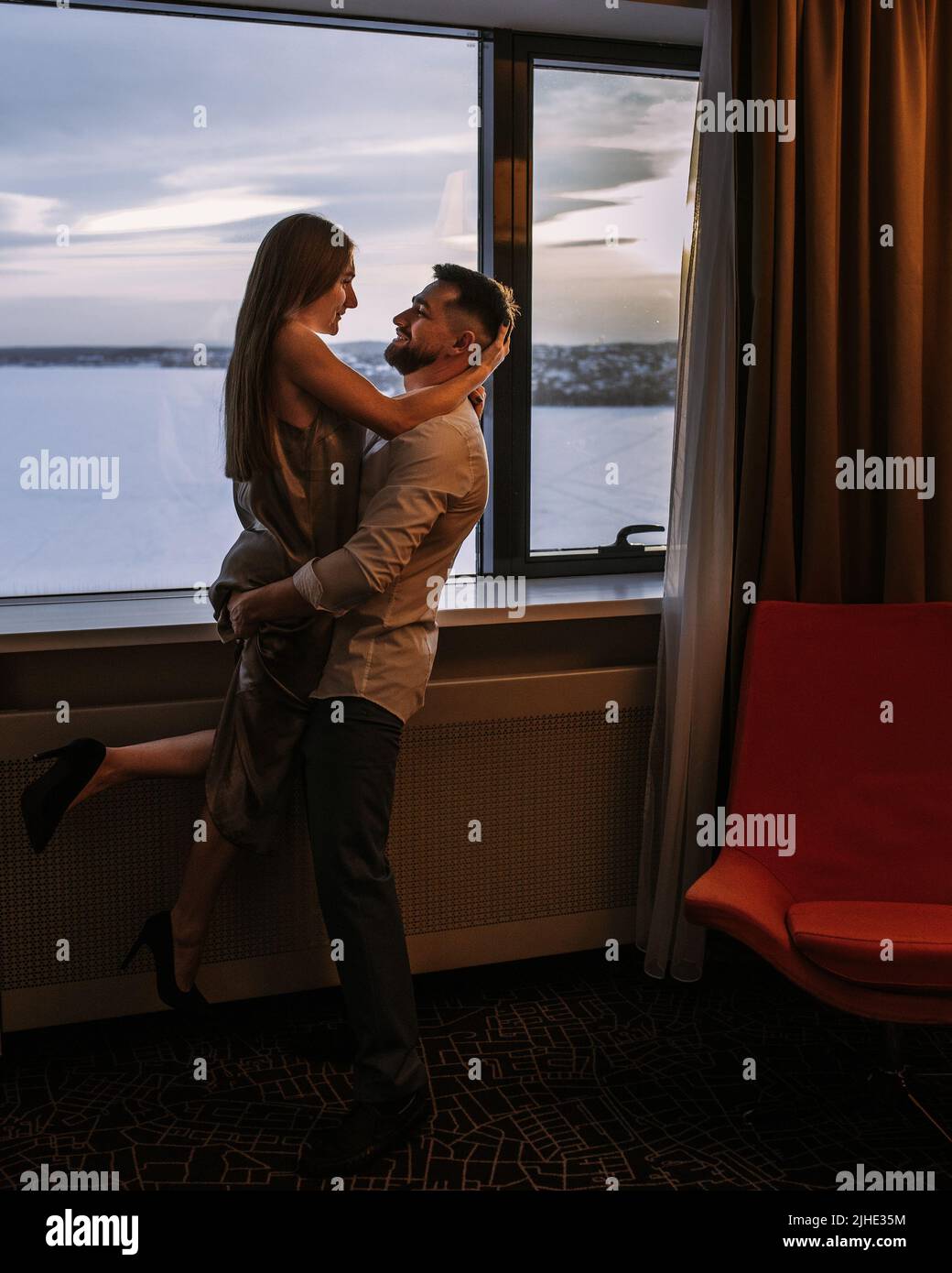 Happy loving couple in hotel standing on window background on sunset ...