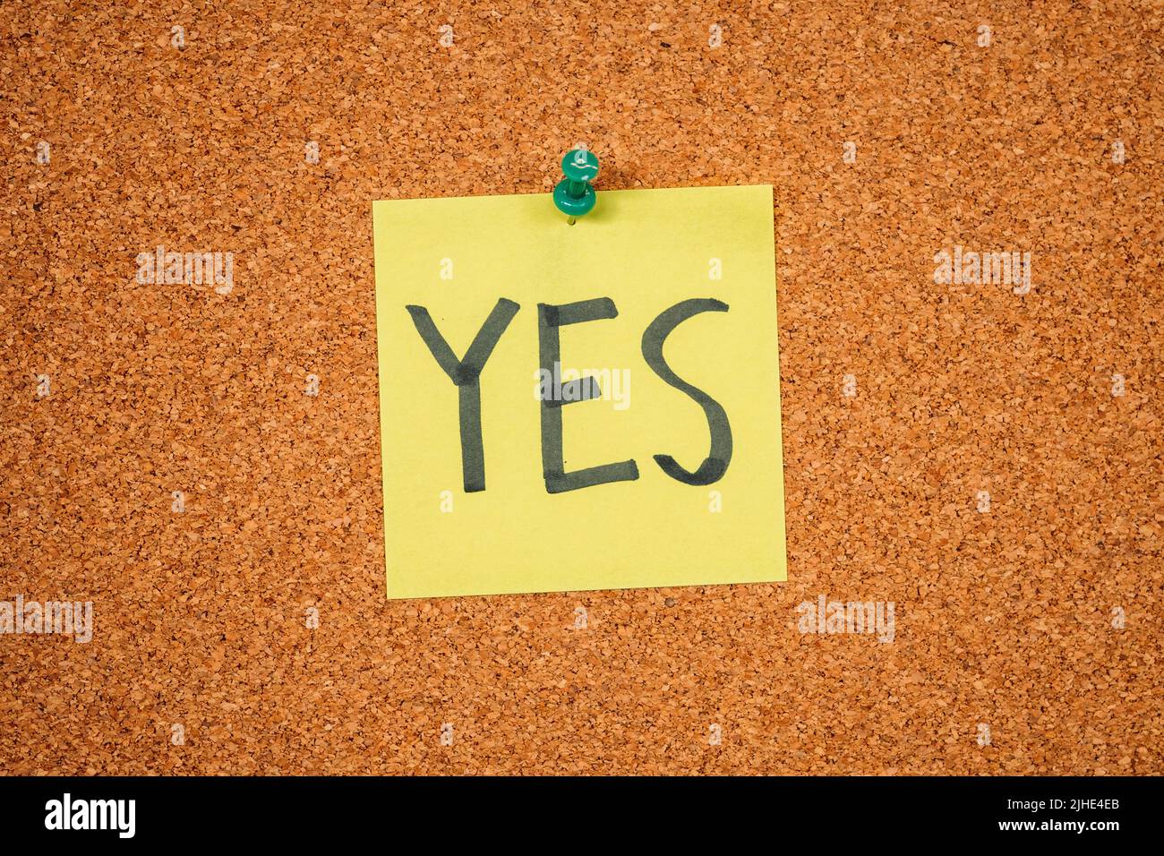 Yellow sticky note on a cork board with drawing pin with the word Yes ...