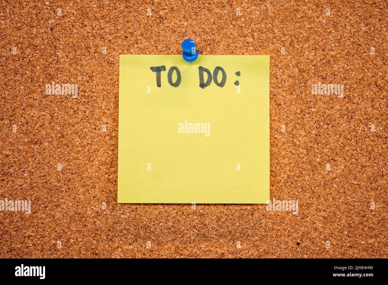 Yellow sticky note on a cork board with drawing pin with the word To do ...