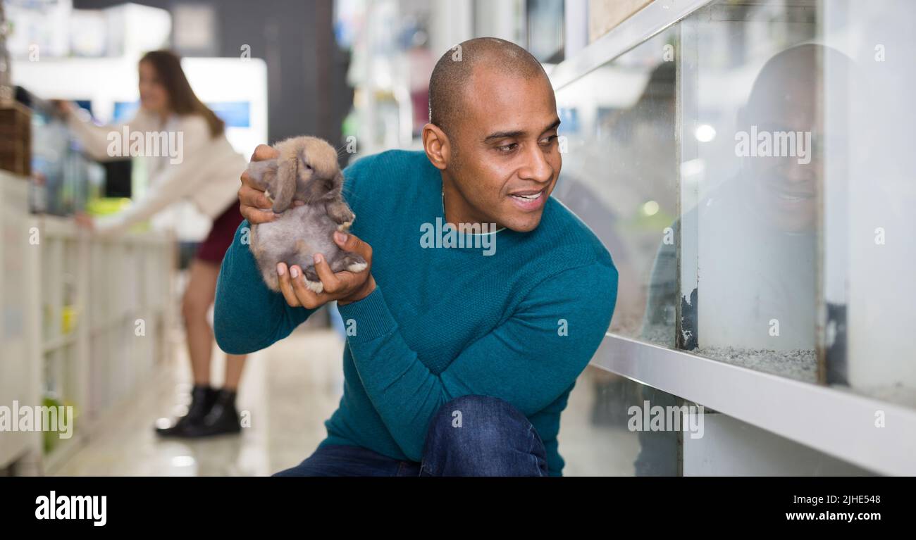 Joyful man tenderly holding a rabbit in his arms in pet store Stock ...