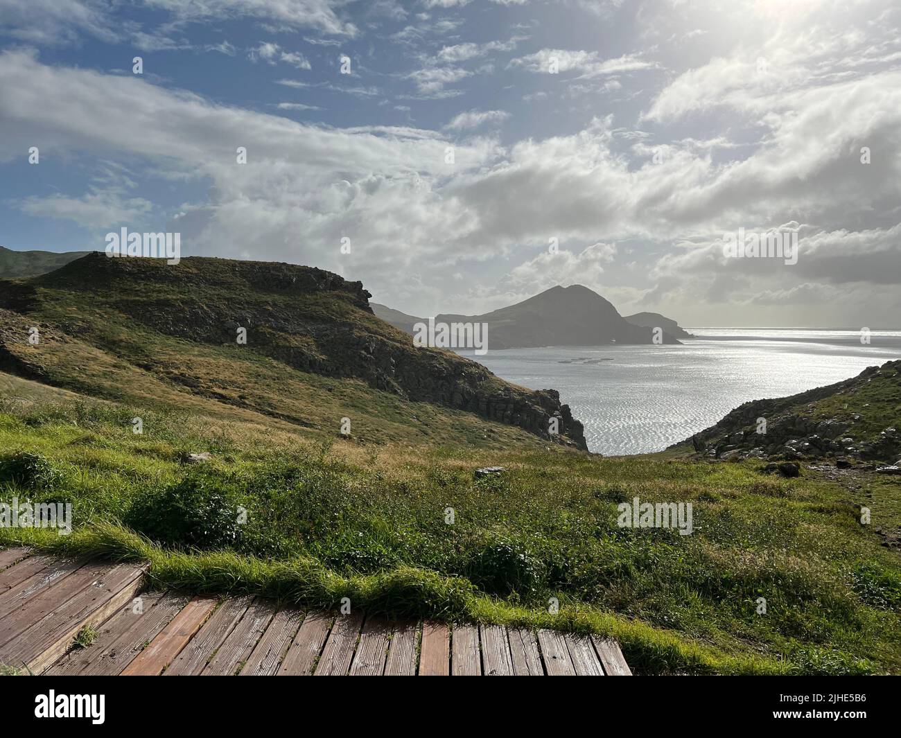 A landscape view of green plains by shiny water under cloudy gray sky ...