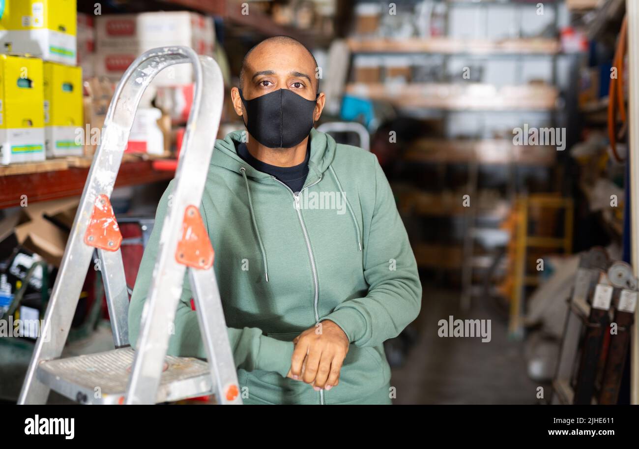 Owner of hardware store in protective mask among shelving with goods ...