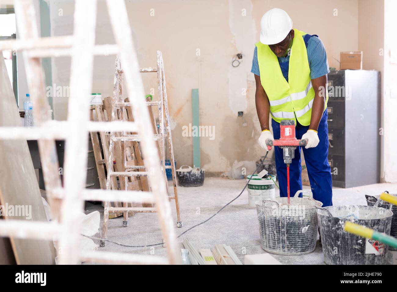 Male builder mixing plaster in bucket using electric mixer closeup ...