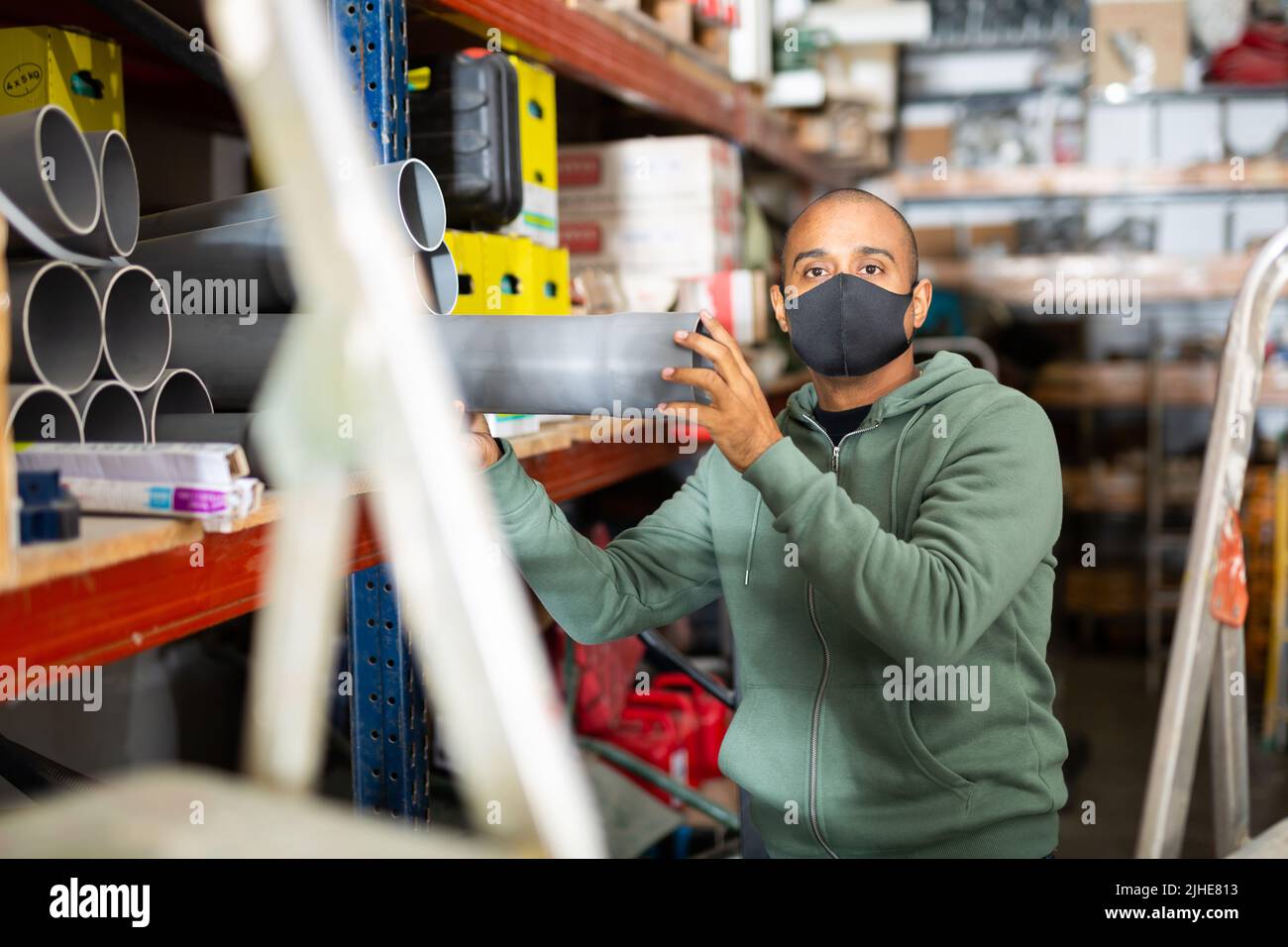 Latin american man in protective mask choosing plastic pipes in store ...
