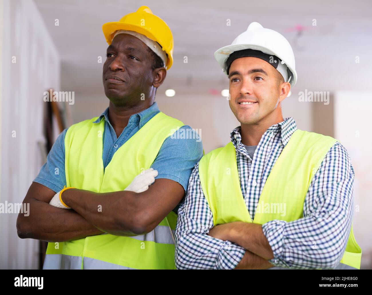 Portrait of two positive builders standing in construction site Stock ...