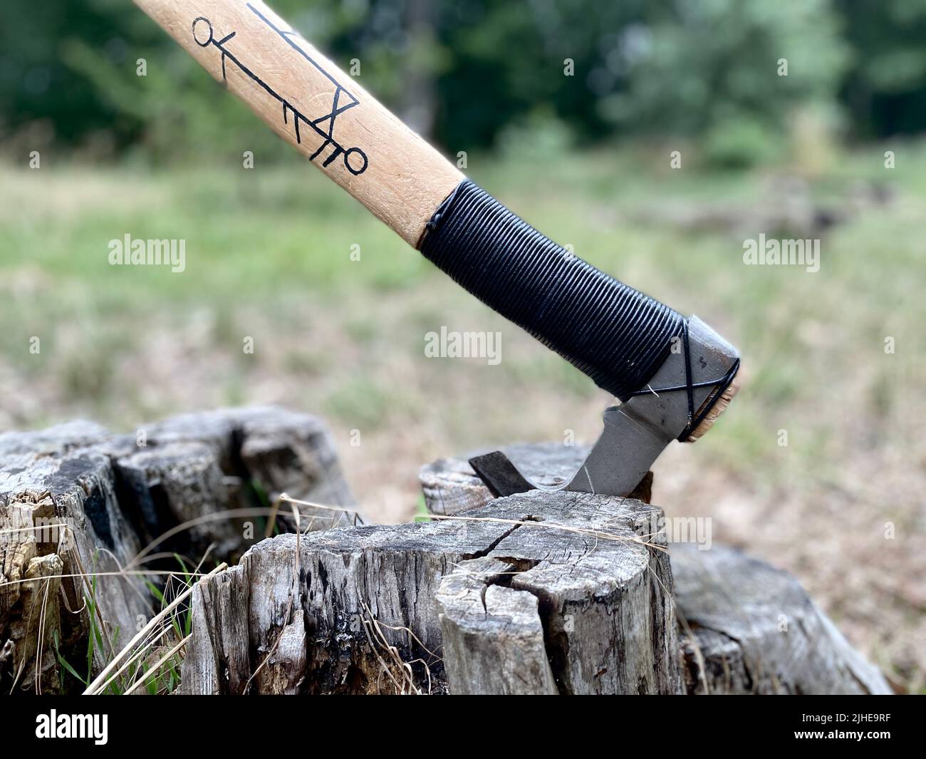 A closeup of a Viking-inspired axe with symbols on a handle stuck in a ...