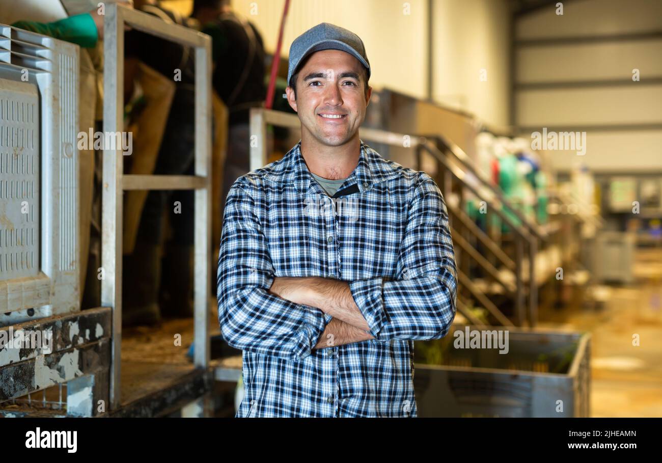 Smiling farmer standing with crossed arms at vegetable sorting factory ...