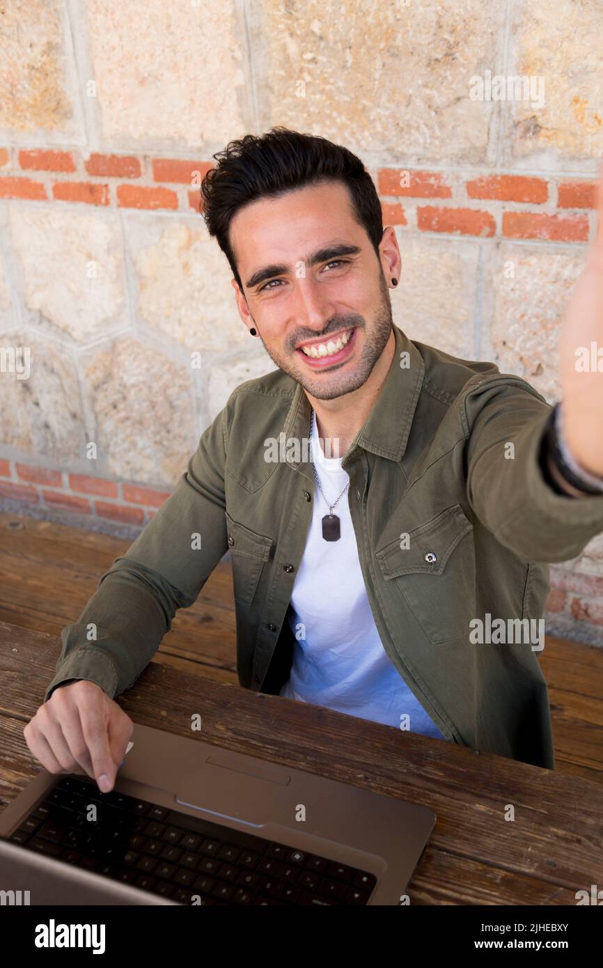 Vertical photo of a man taking a selfie while working with a laptop on ...