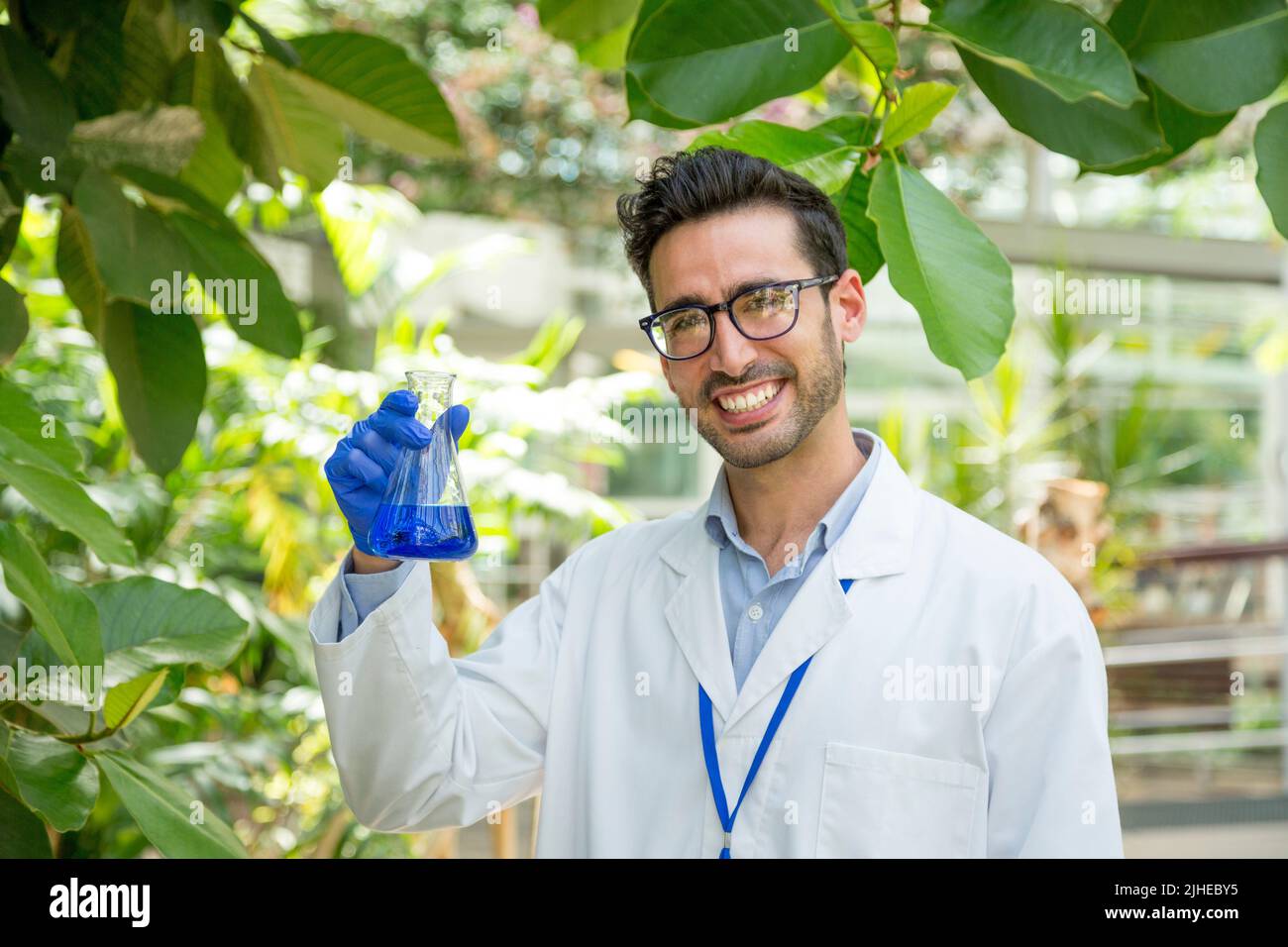 Biologist showing a lab flask with blue chemical liquid next to plants ...