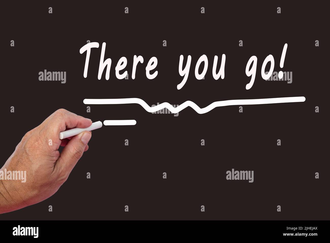 Male hand writes in white chalk pencil the word THERE YOU GO on a black ...