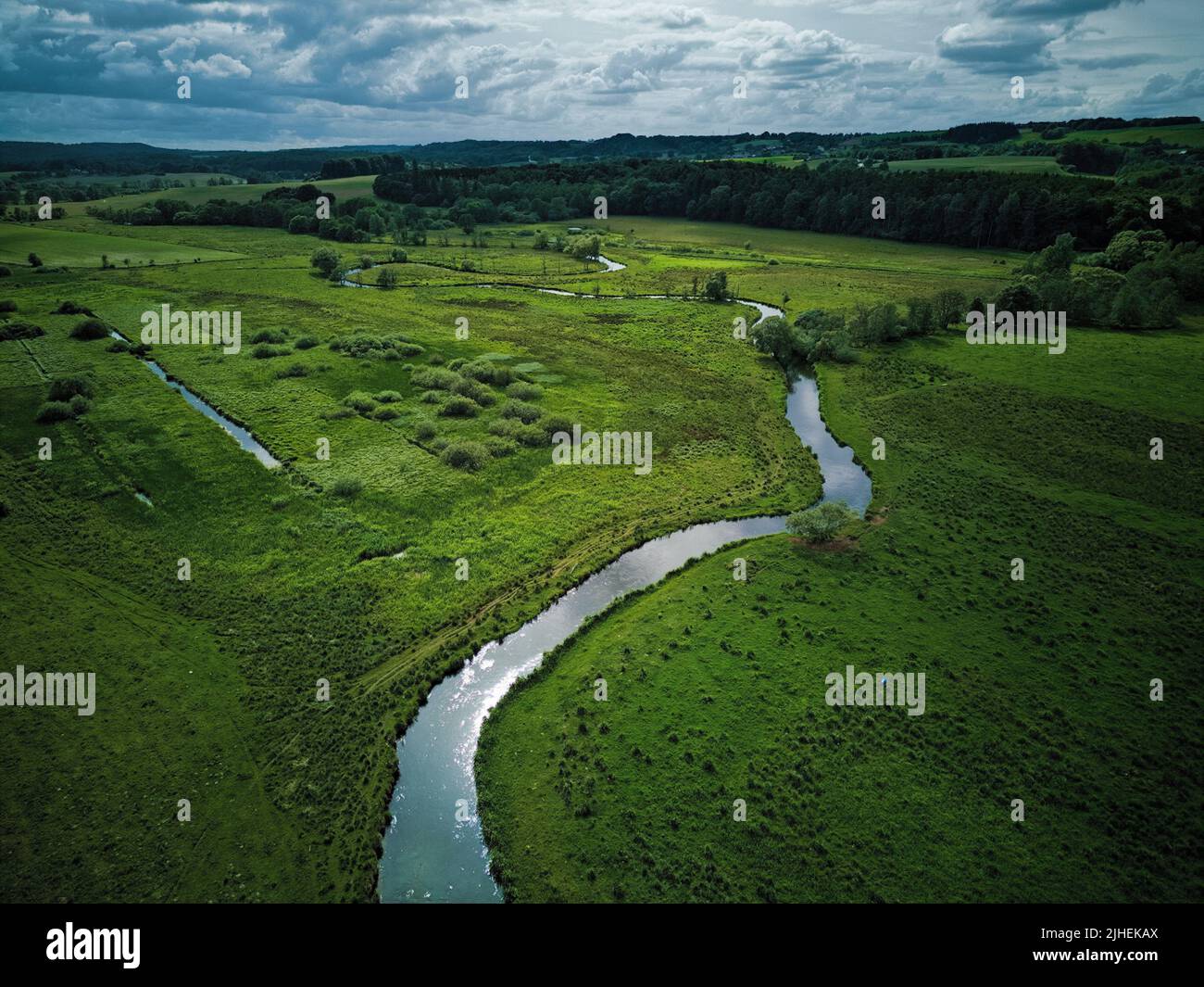 An aerial view of long narrow river flowing through lush green fields ...