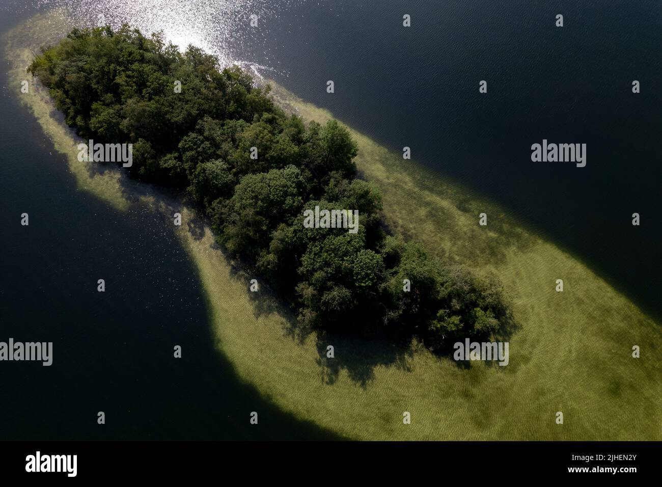 Sunspot reflection in the water of green island top down aerial view in ...