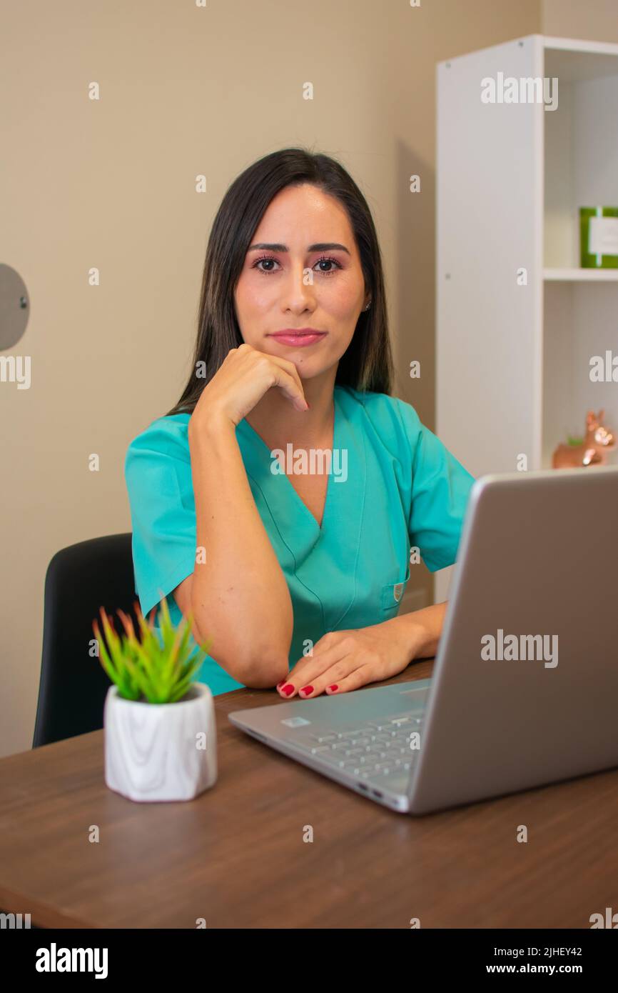 A vertical shot of young female nurse in green uniform by her desk with ...