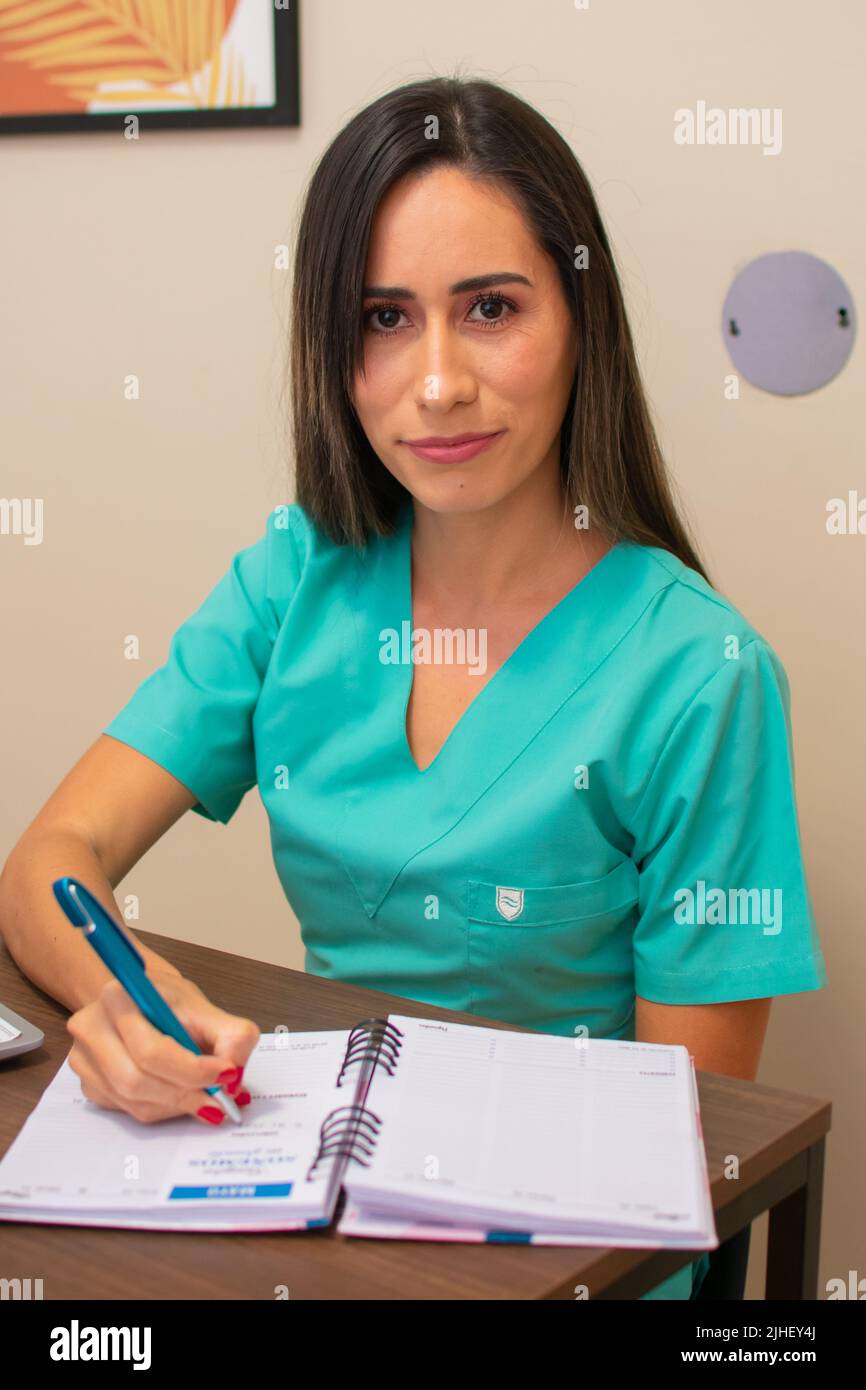 A vertical shot of young female nurse in green uniform taking notes in ...