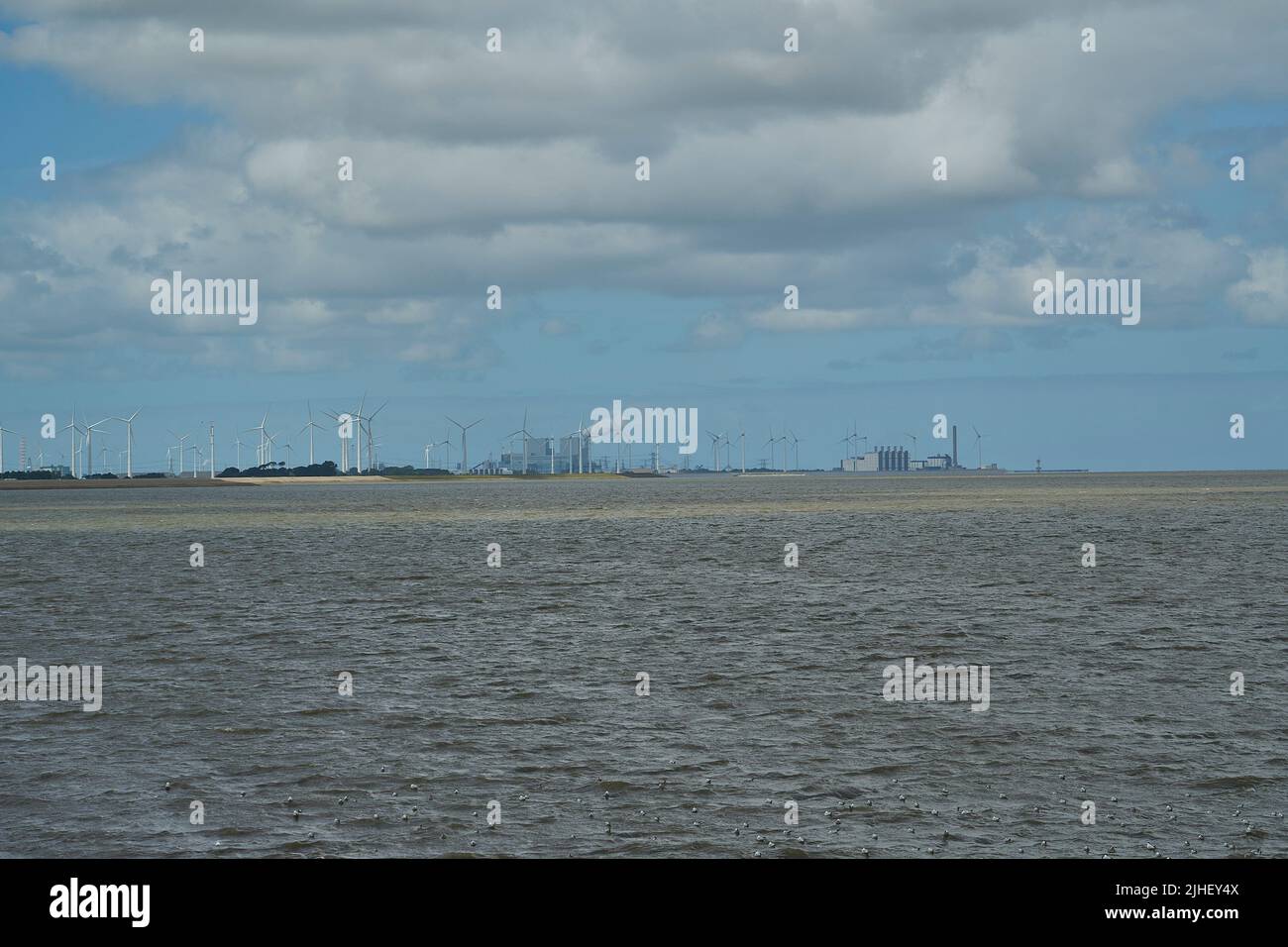 Wind turbines of a power plant standing on a dike at industrial complex ...