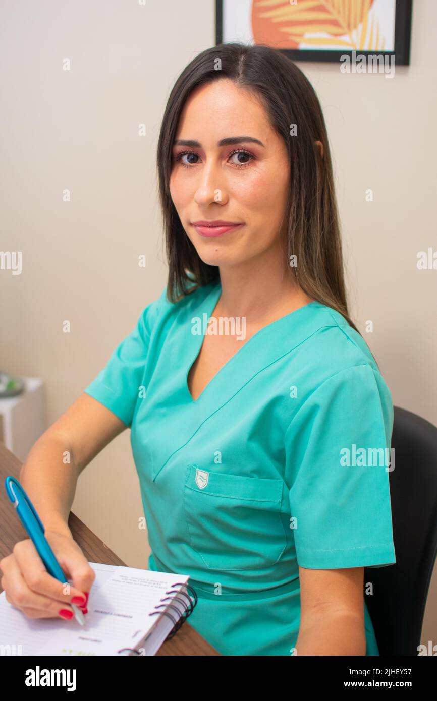 A vertical shot of young female nurse in green uniform taking notes in ...
