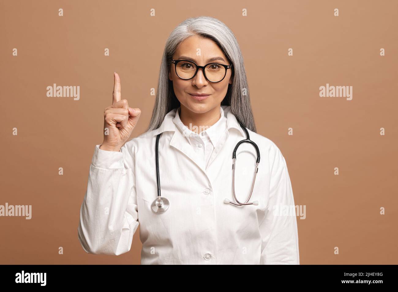 Smiling mature gray-haired Asian female doctor in white medical gown ...