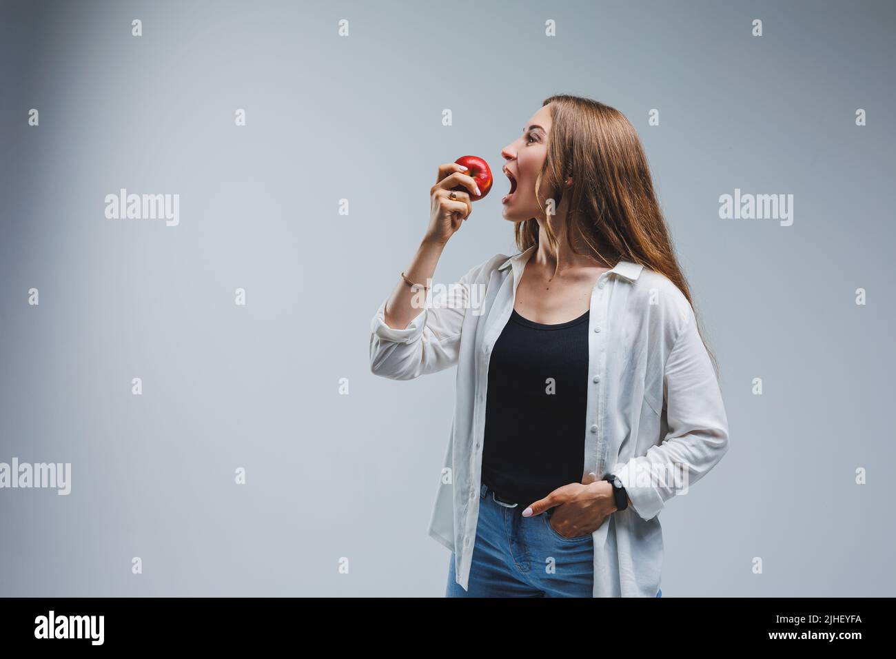Cute Brunette Woman In White Shirt Holding Red Apple In Hand Standing