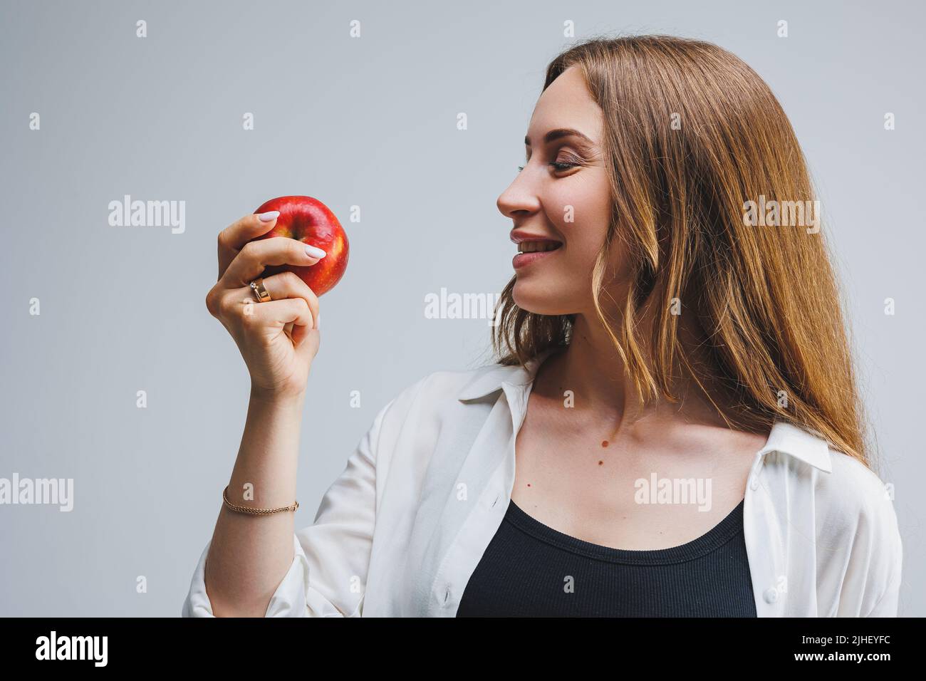 Cute Brunette Woman In White Shirt Holding Red Apple In Hand Standing
