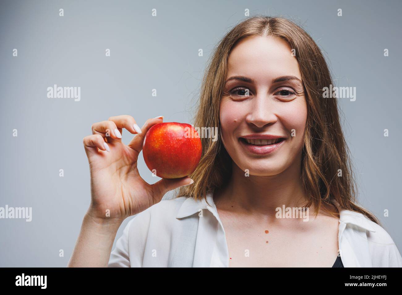 Cute Brunette Woman In White Shirt Holding Red Apple In Hand Standing