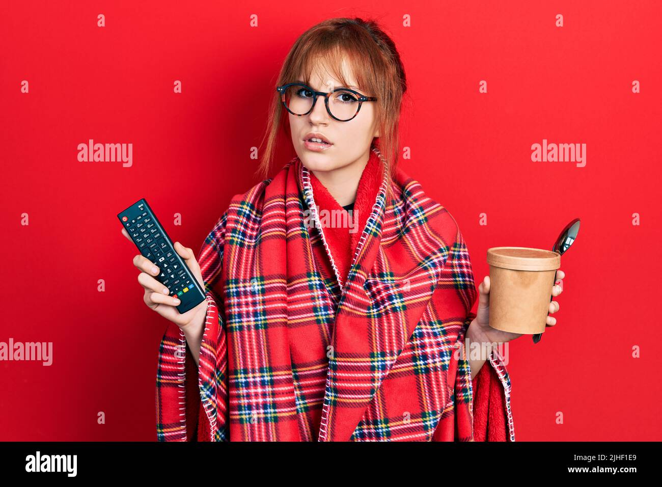 Redhead young woman wrapped in a red warm red blanket eating icecream ...