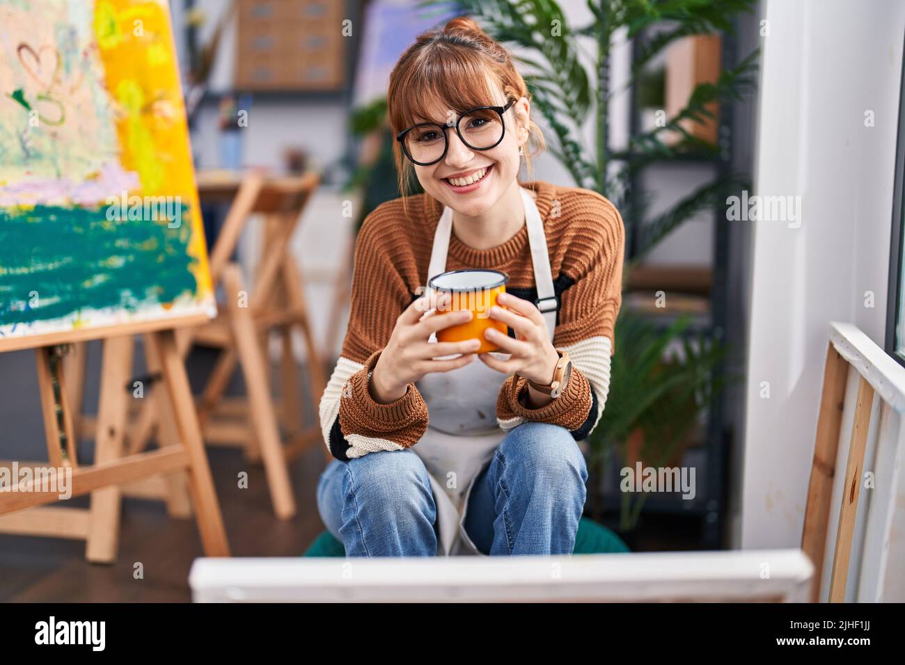Young woman artist smiling confident drinking coffee at art studio ...