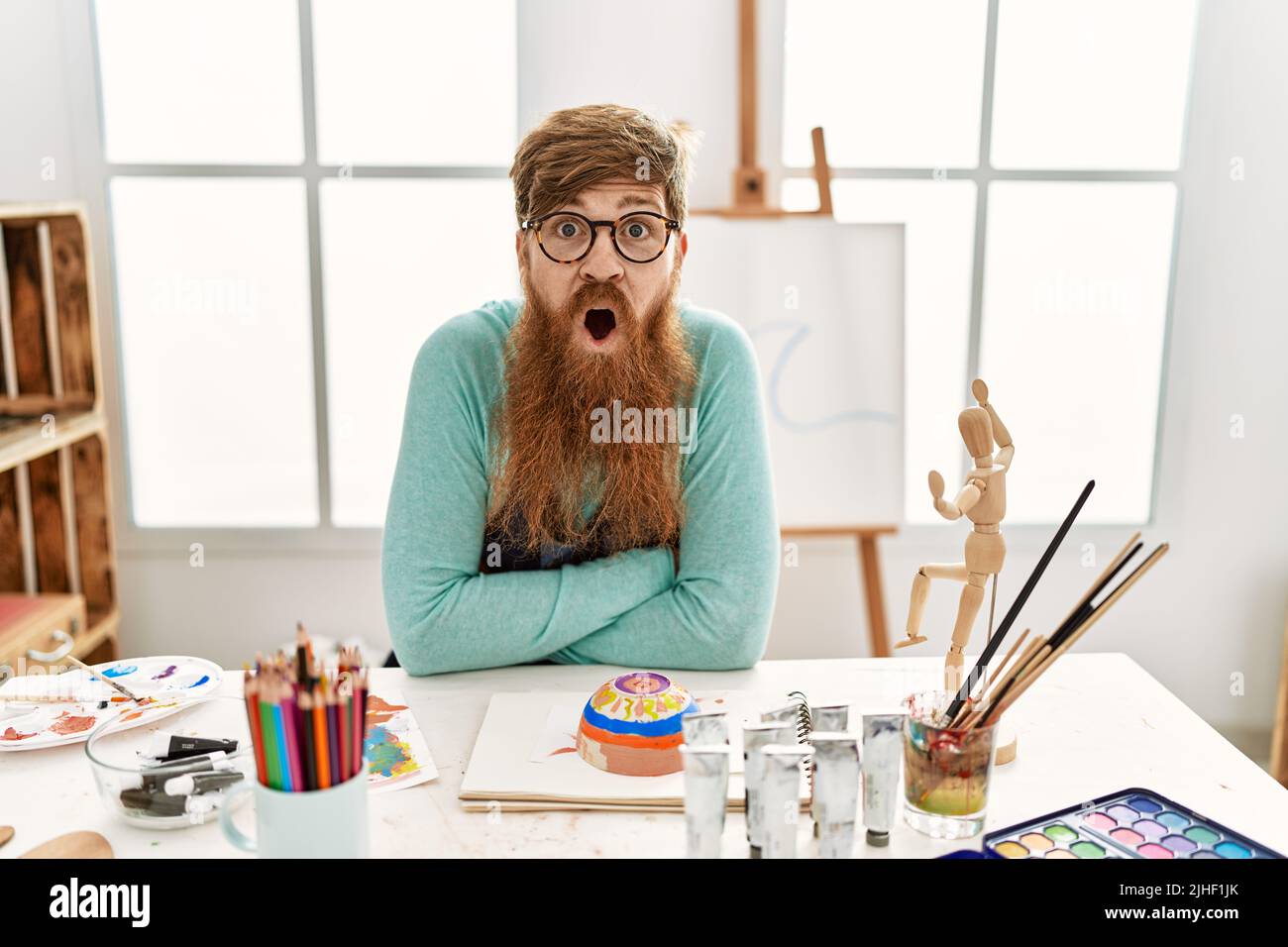 Redhead man with long beard painting clay bowl at art studio afraid and ...