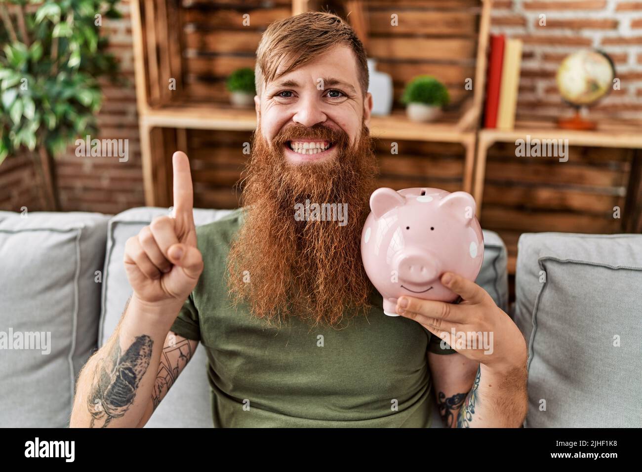 Redhead man holding piggy bank smiling with an idea or question ...